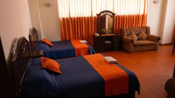 Quarto de hotel com duas camas, uma escrivaninha, uma cadeira, um espelho e uma janela com cortinas.