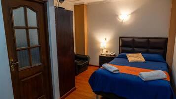 Quarto com cama, mesa de cabeceira, abajur, guarda-roupa e porta.
