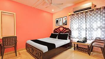 Quarto de hotel com cama, escrivaninha, cadeira, aparelho de ar condicionado e ventoinha de teto.