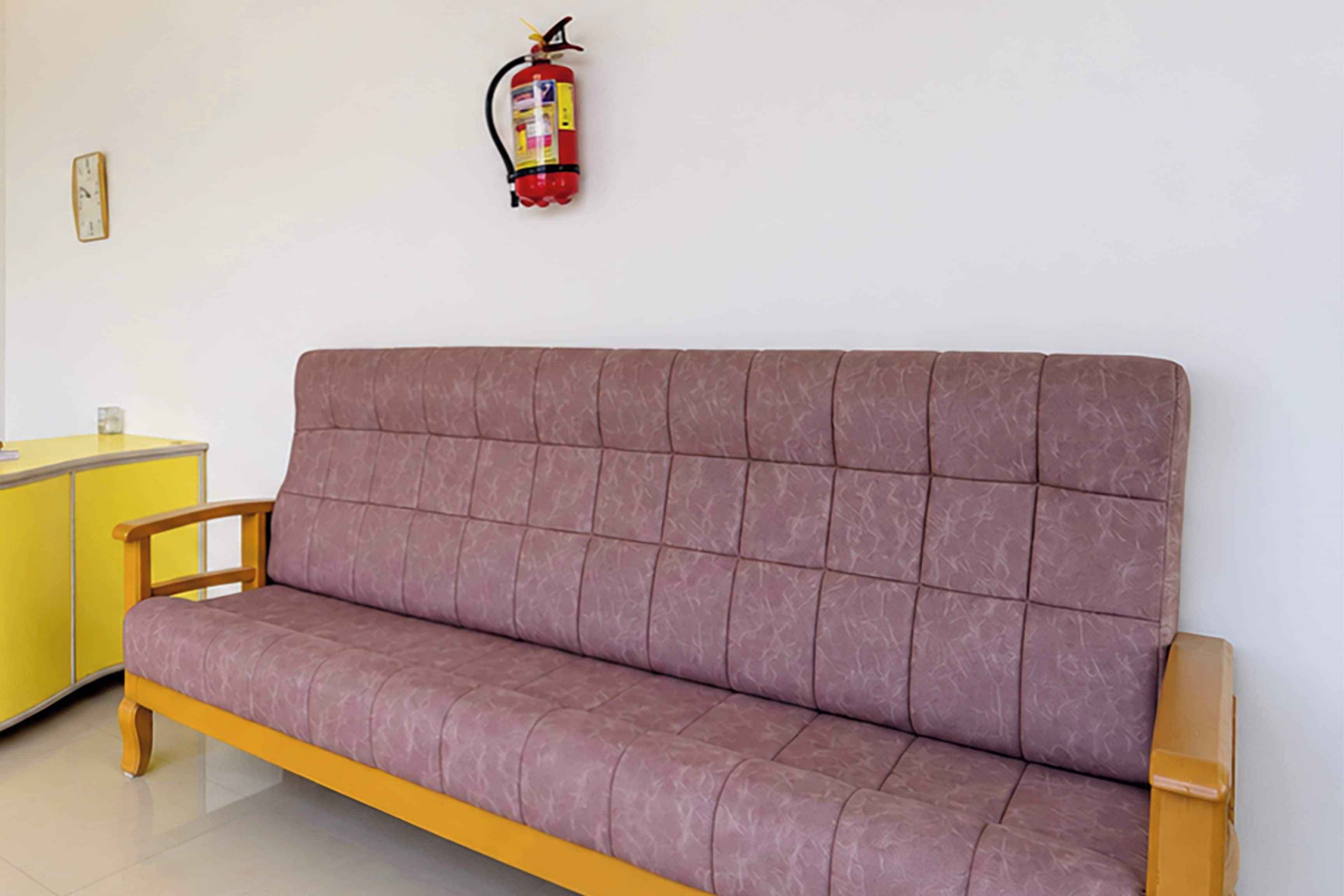 Quarto com sofá, uma mesinha e um extintor de incêndio na parede.