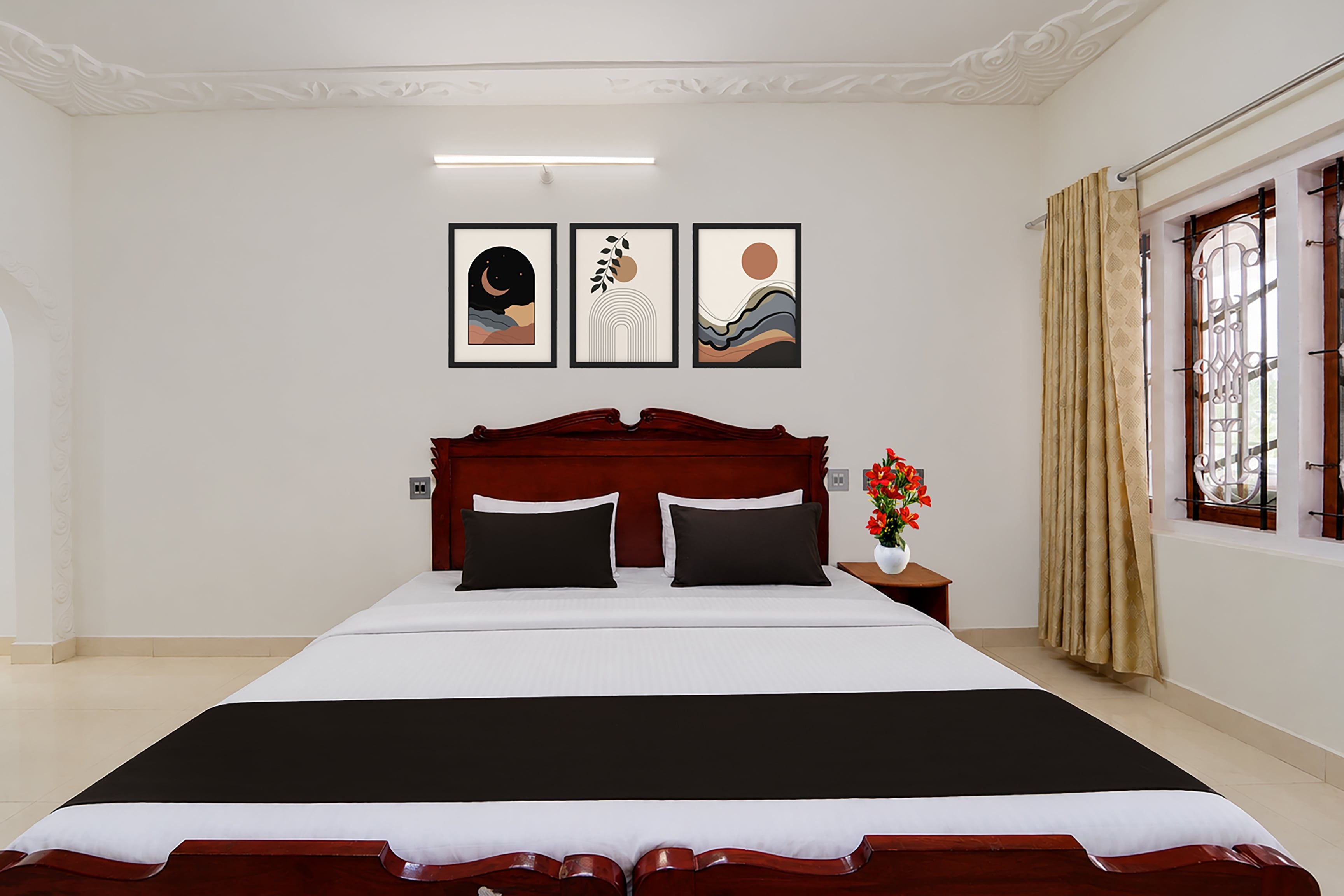 Quarto com uma cama grande, uma mesa de cabeceira com um vaso de flores e três obras de arte emolduradas na parede.