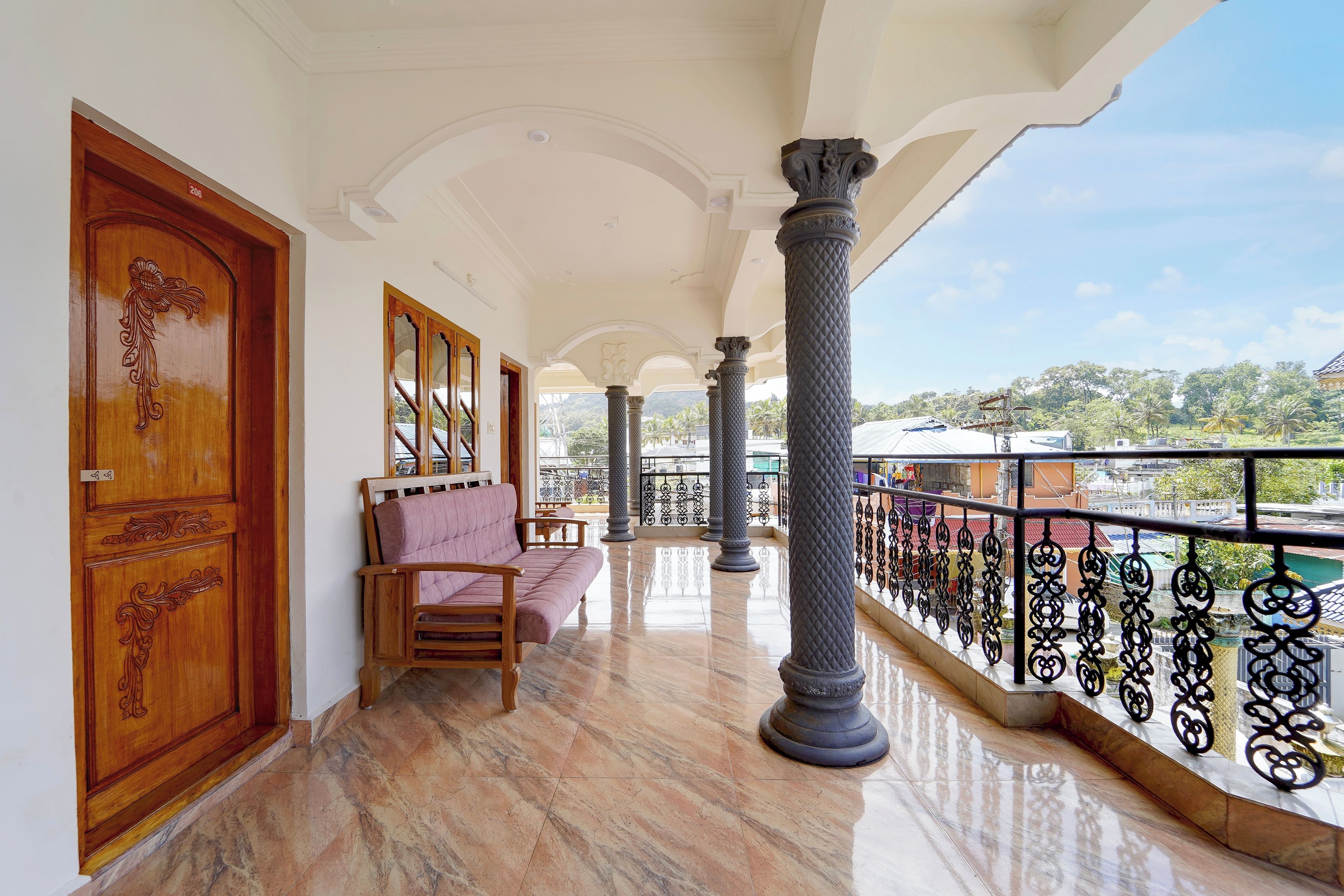 Varanda ampla com piso de mármore, porta de madeira com detalhes entalhados e vista para uma paisagem exuberante.