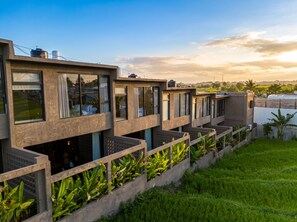 Uma fileira de edifícios residenciais modernos, com vários andares, grandes janelas e varandas, rodeada por vegetação exuberante.