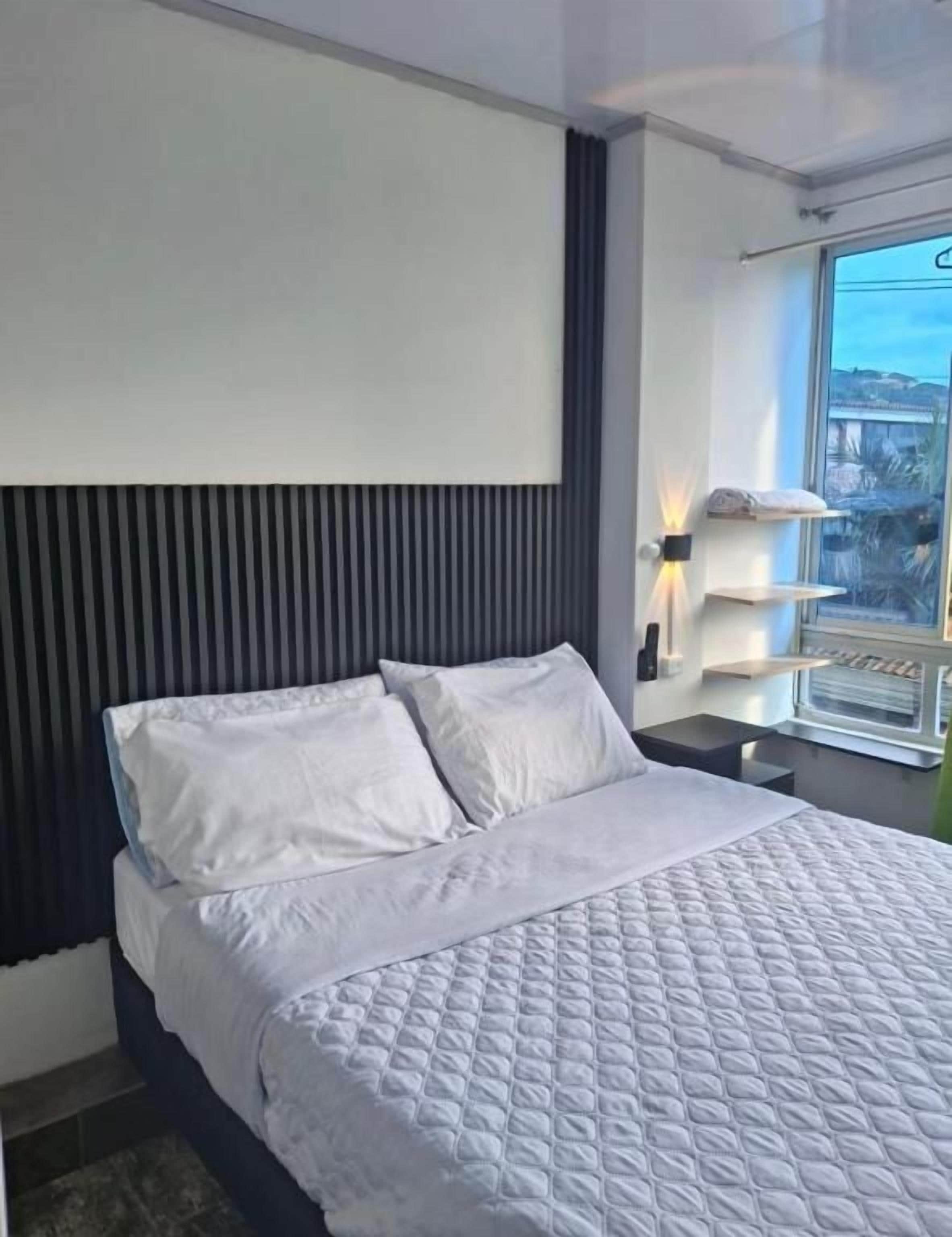 Quarto moderno com cama, mesas de cabeceira e janela com vista.
