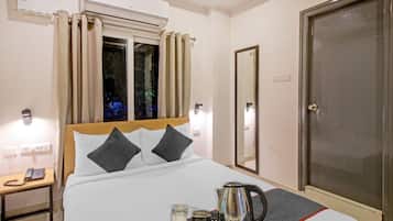 Quarto de hotel com cama, mesa de cabeceira com telefone, janela com cortinas, ar condicionado, porta e espelho.