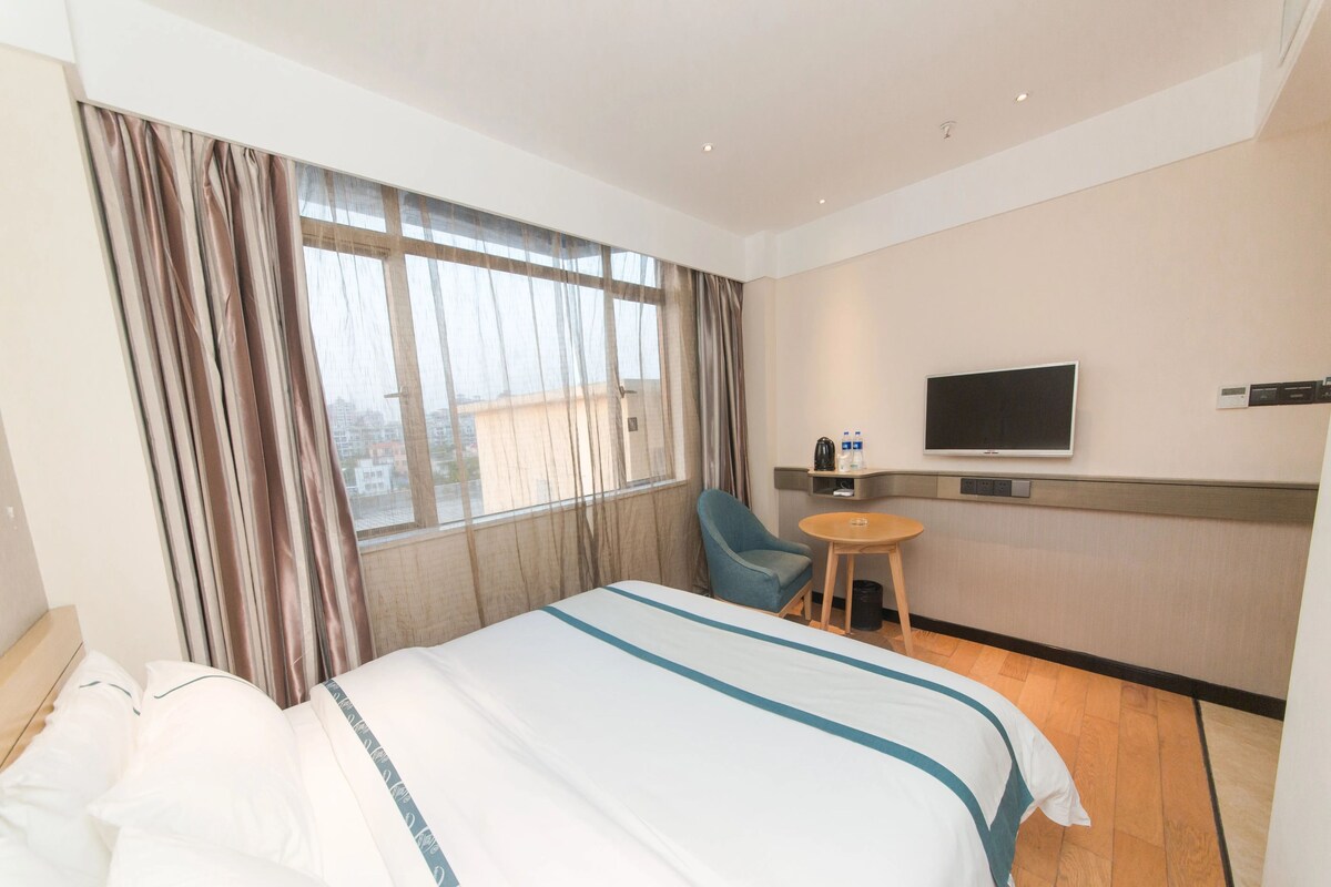 Quarto de hotel com uma cama, televisão, mesinha e uma cadeira.