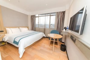 Quarto de hotel com cama, mesa pequena, cadeira, televisão e janela com cortinas.