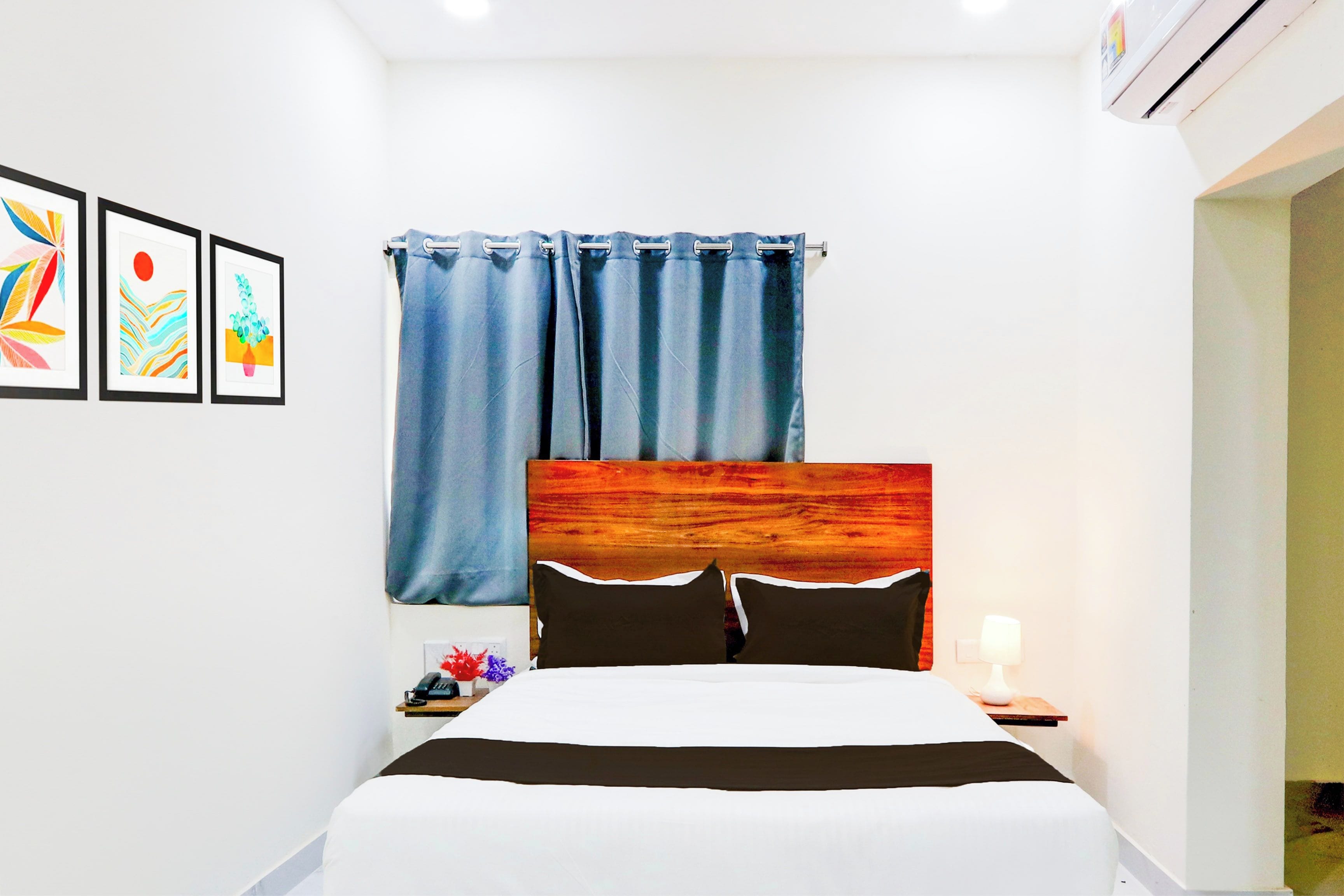 Quarto de hotel com cama, mesa de cabeceira, luminária e ar-condicionado fixado na parede.