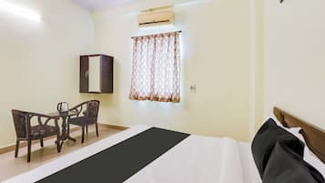 Quarto de hotel com cama, escrivaninha, cadeira, ar condicionado e janela com cortinas estampadas.