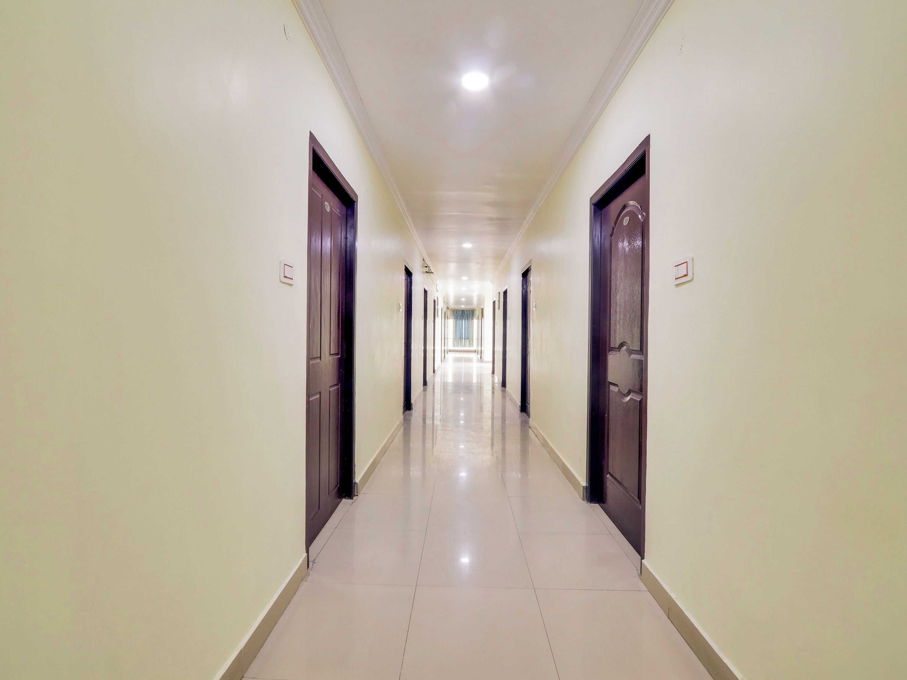 Um corredor longo e bem iluminado, com portas em ambos os lados, que leva a um quarto claro no final.