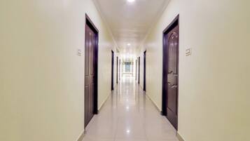 Um corredor longo e bem iluminado, com portas em ambos os lados, que leva a um quarto claro no final.