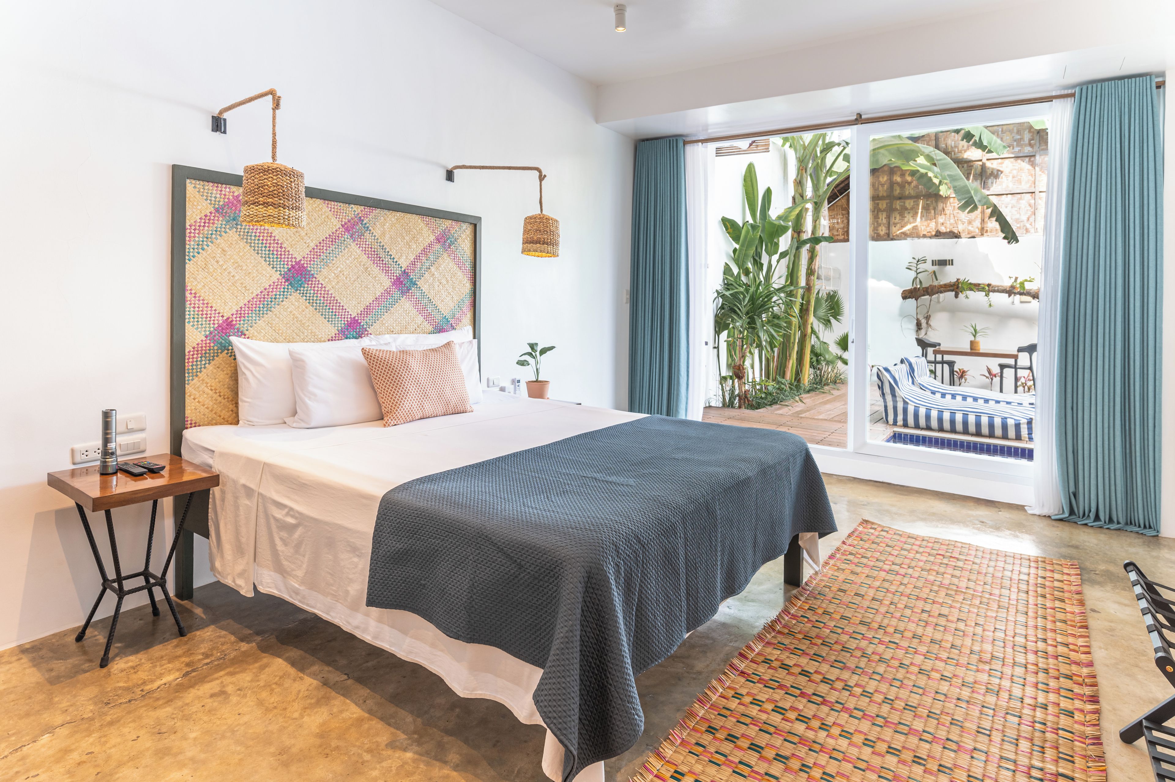 Quarto com cama, mesa de cabeceira e vista para a área externa.