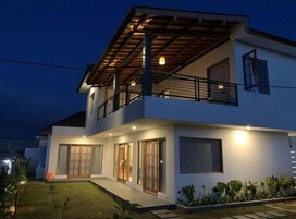 Uma casa moderna de dois andares, com varanda, janelas amplas e fachada bem iluminada.