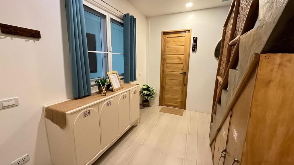 Um corredor com porta de madeira, janela com cortinas azuis, armário com moldura de quadro e planta em vaso.