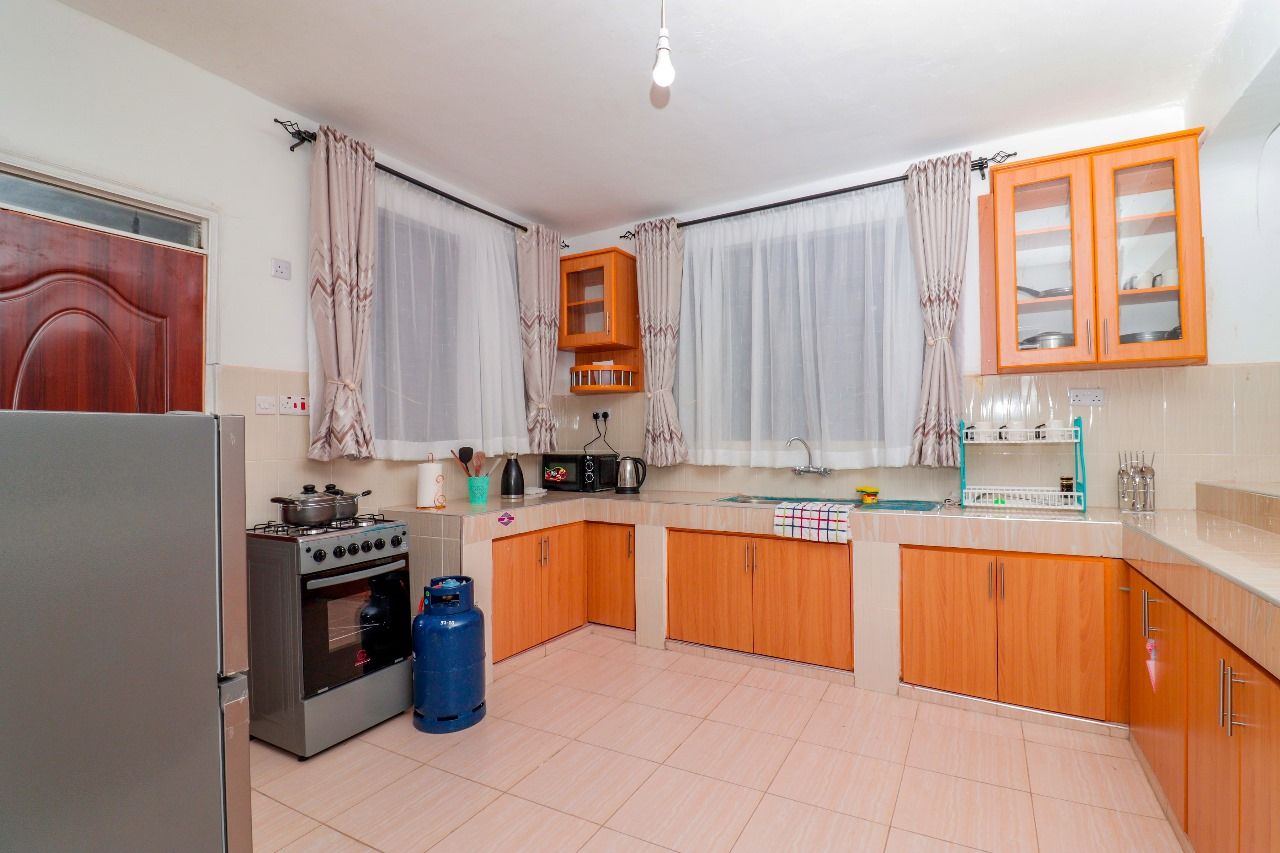 Cozinha com armários de madeira, fogão a gás, geladeira e cilindro de gás azul.