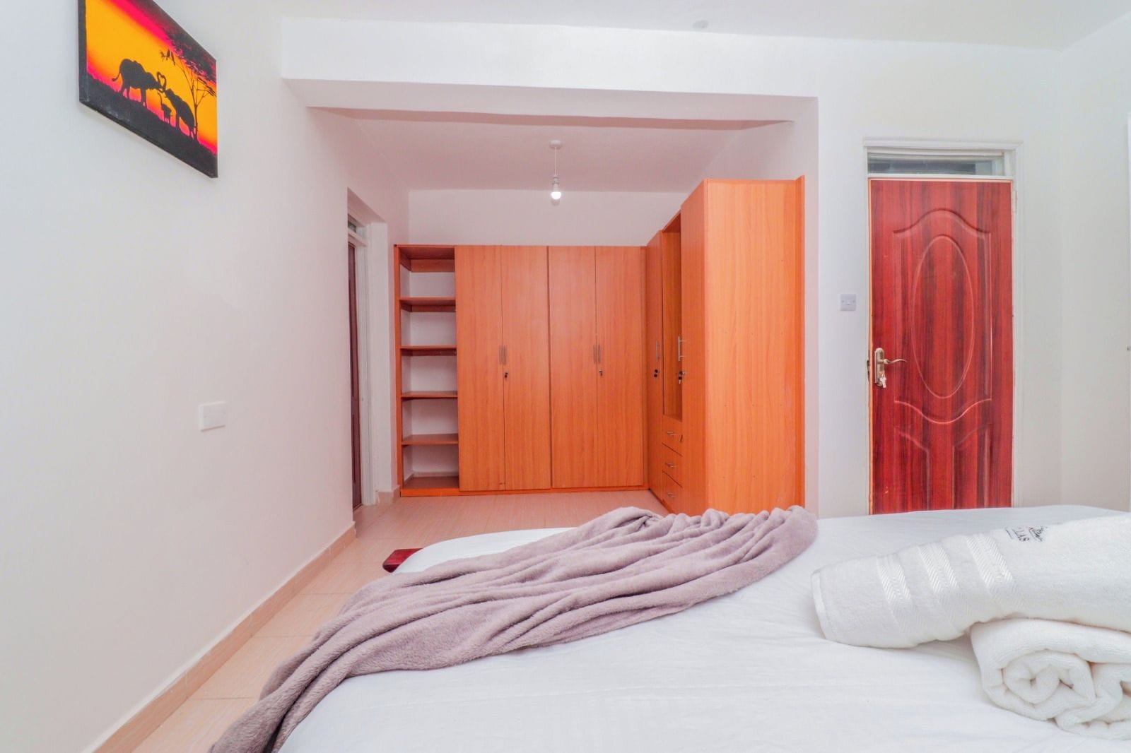 Quarto com cama, guarda-roupa, porta e um quadro na parede.