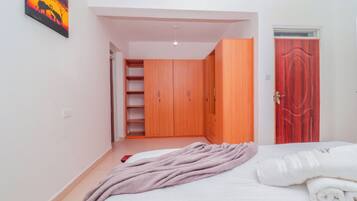 Quarto com cama, guarda-roupa, porta e um quadro na parede.