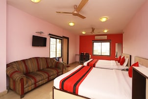 Quarto de hotel com sofá, duas camas, televisão, ventoinhas de teto e ar condicionado.
