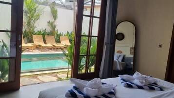 Quarto de hotel com cama, uma janela grande e vista para uma piscina.