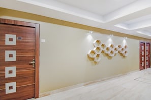 Um corredor com porta de madeira à esquerda, luminária na parede e decoração geométrica.
