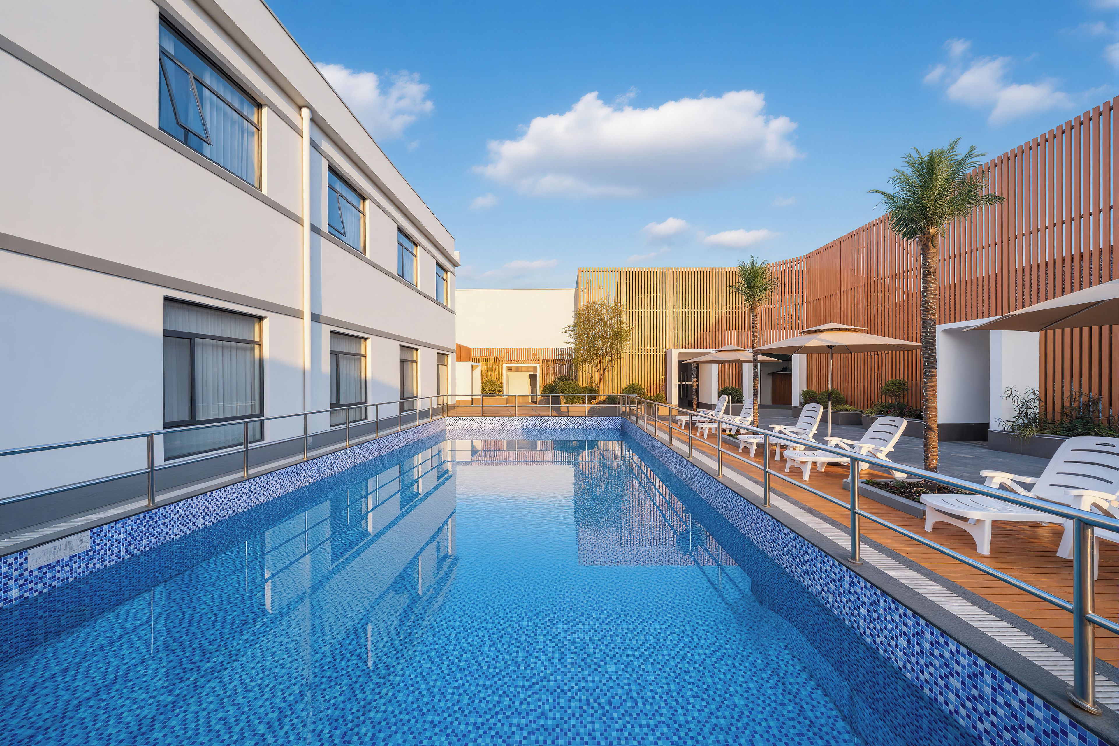 Uma área de piscina moderna de hotel, piscina azul límpida, espreguiçadeiras e cerca de madeira.