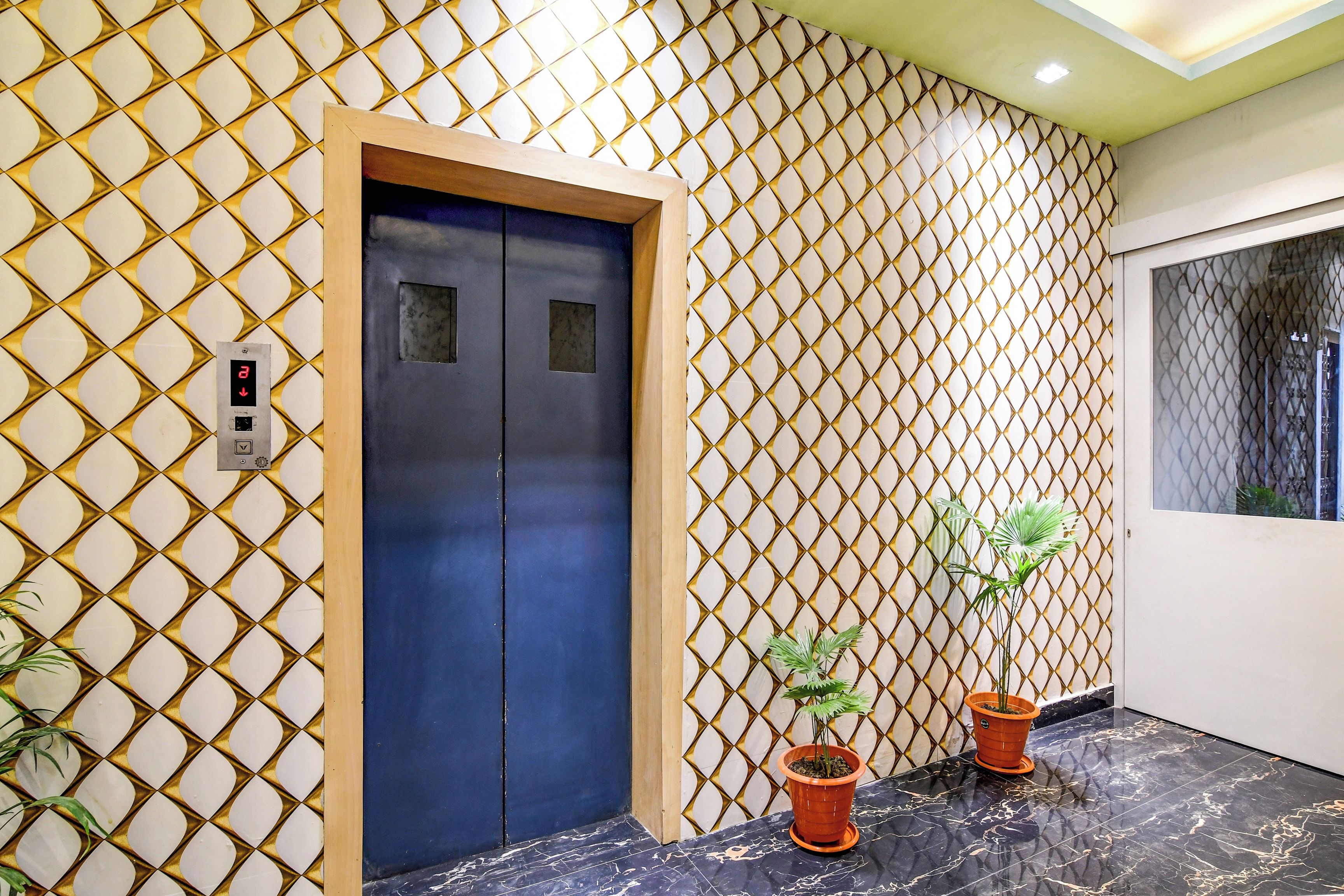 Um elevador com visor digital, parede estampada e plantas em vasos.