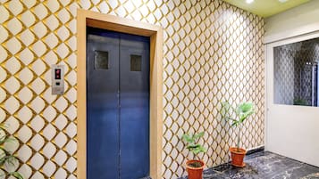 Um elevador com visor digital, parede estampada e plantas em vasos.