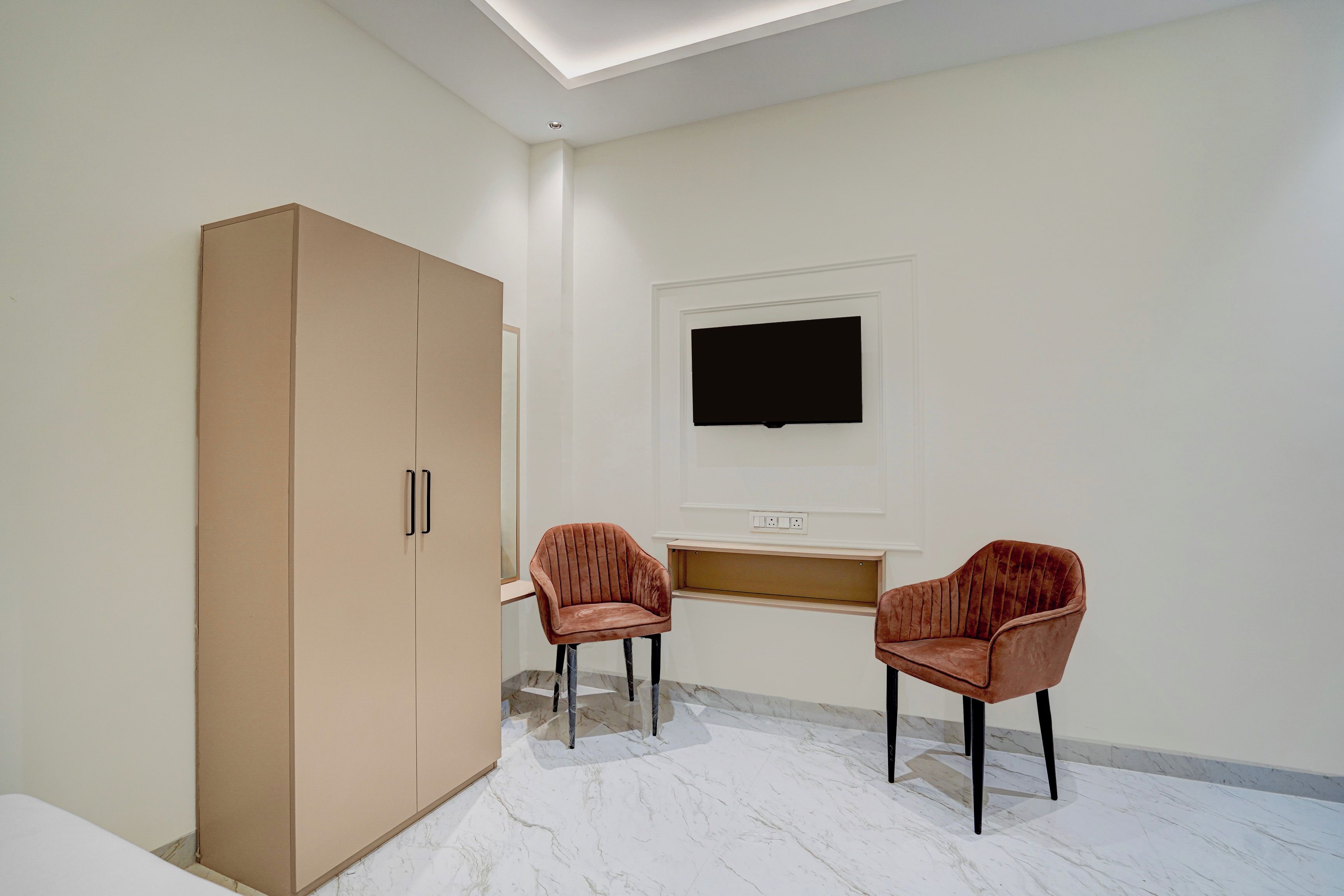 Quarto com guarda-roupa, duas cadeiras, televisão e piso de mármore.
