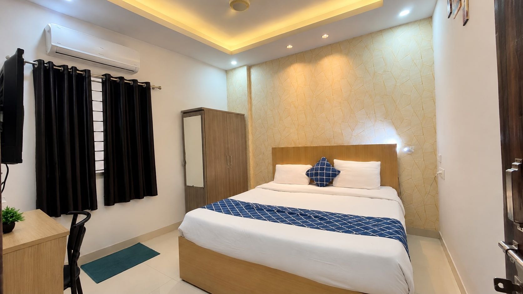 Quarto de hotel com cama, guarda-roupa, escrivaninha e cortina.