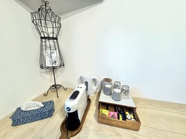 Quarto com mesa de madeira, chaleira elétrica branca, caixa de lenços, caneca e xícara, além de uma gaveta com diversos objetos.