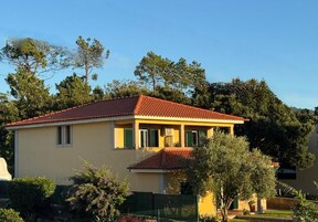 Um edifício de dois andares com telhado de telhas vermelhas, cercado por vegetação e árvores.