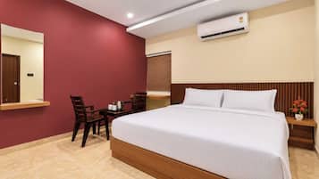 Quarto de hotel com cama, escrivaninha, cadeira, espelho e ar condicionado.
