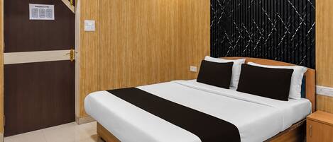 Quarto de hotel com piso de madeira, cama com roupa de cama branca e preta, mesa de cabeceira de madeira, parede texturizada preta e uma porta com um aviso.