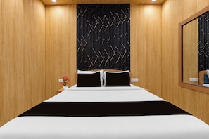 Quarto de hotel com uma cama grande, paredes de madeira, painel de parede preto e branco estampado, mesa de cabeceira com um vaso de flores e espelho na parede.