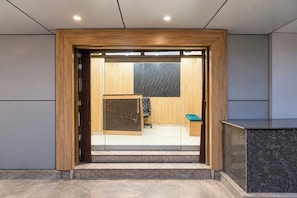 Interior moderno com entrada emoldurada em madeira, porta de vidro e balcão de recepção.