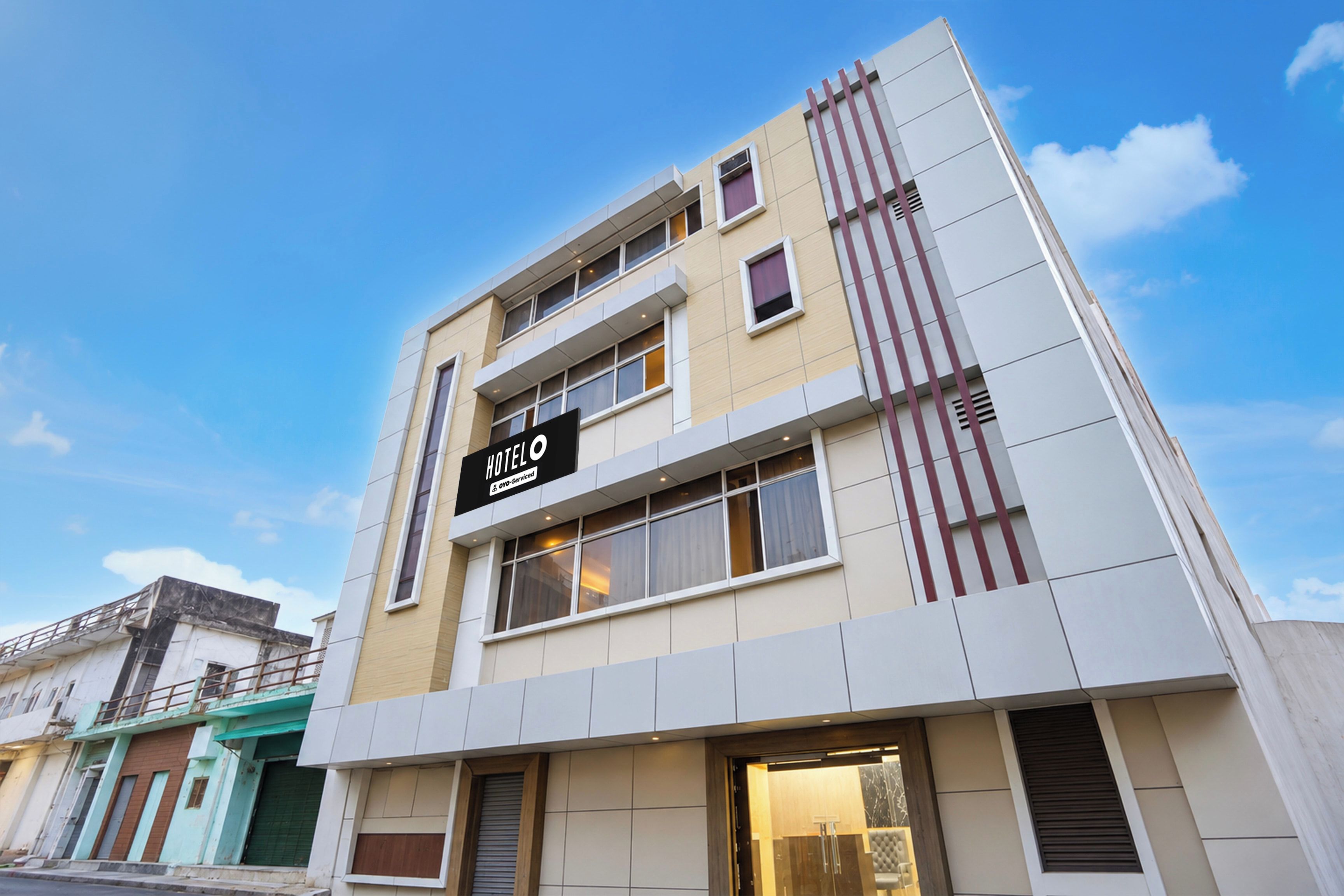 Hotel com fachada moderna, placa visível indicando serviço OYO e céu claro ao fundo.