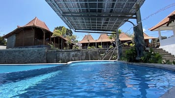 Piscina com parede de pedra e área coberta com telhado metálico.