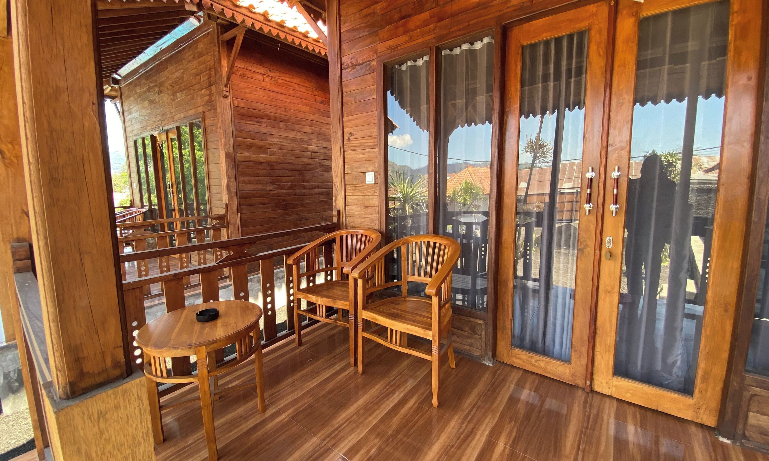 Varanda de madeira com mesa, cadeiras, porta de vidro e vista para o exterior.