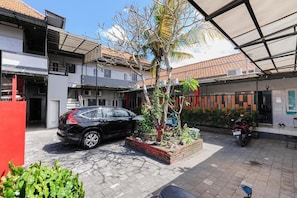 Um pátio com um carro estacionado, uma palmeira e um edifício com telhado de cerâmica.