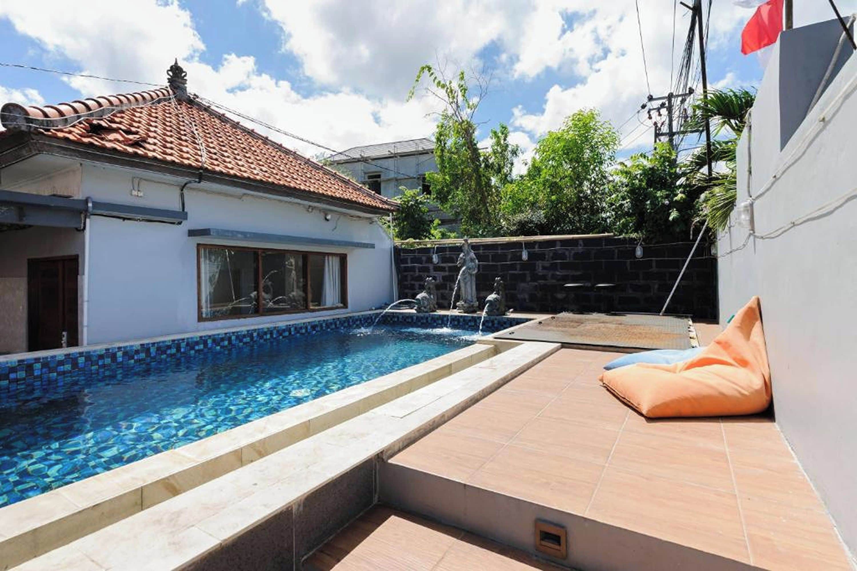 Piscina com borda azulejada, parede de pedra e uma estátua.