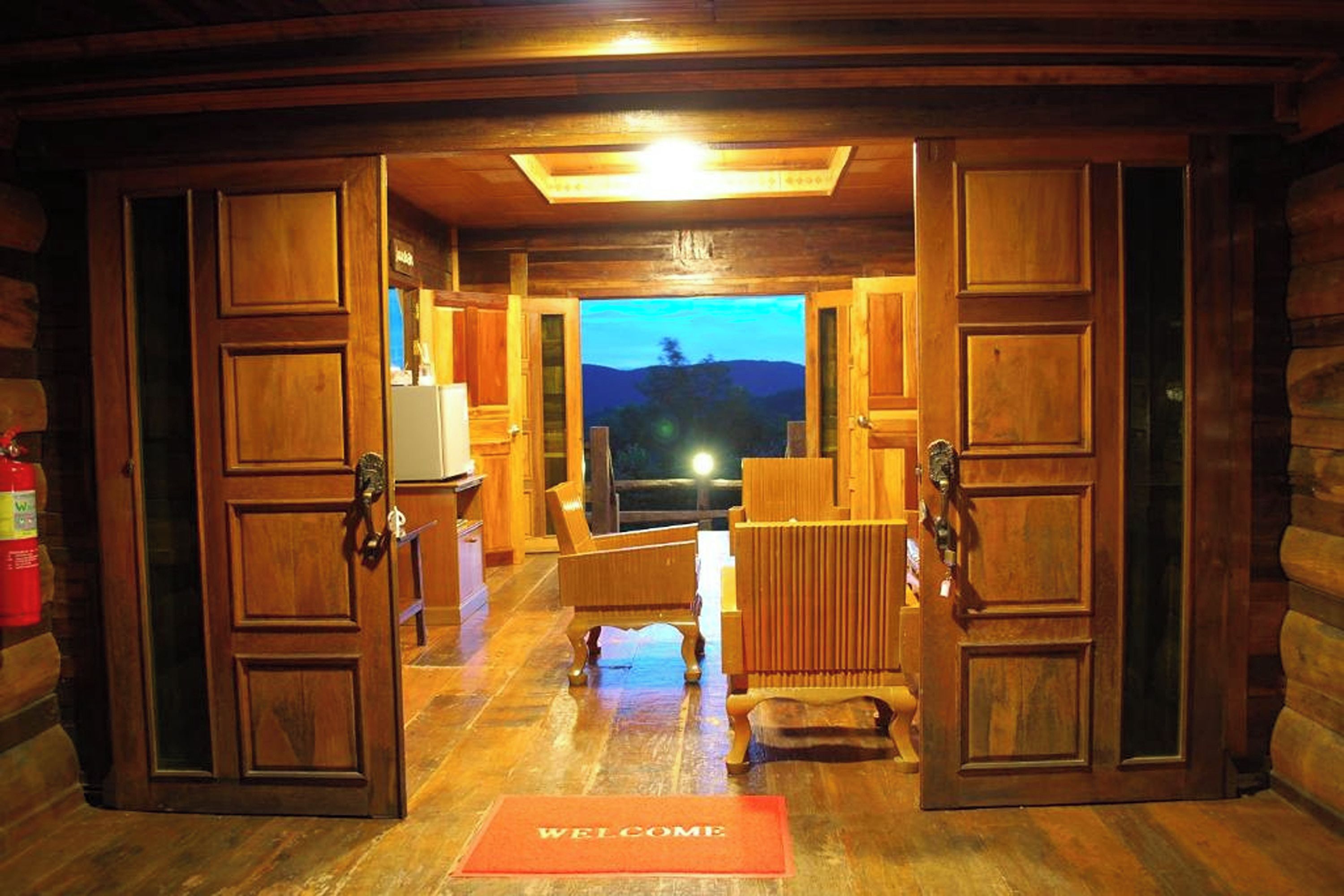 Interior de madeira com tapete de boas-vindas, lareira e vista para o exterior.