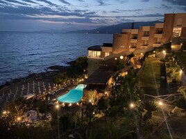 Um hotel à beira-mar com piscina, guarda-sóis na praia e vista para o mar.