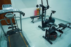 Academia com equipamentos de cardio, aparelhos de musculação e um banco.