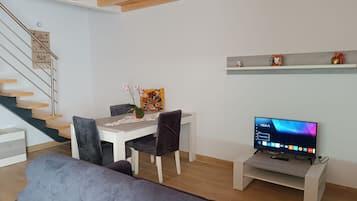 Uma sala de estar moderna com área de jantar, escada e TV sobre suporte.
