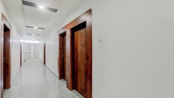 Um corredor com portas de madeira e paredes brancas, que leva a um quarto claro no final.