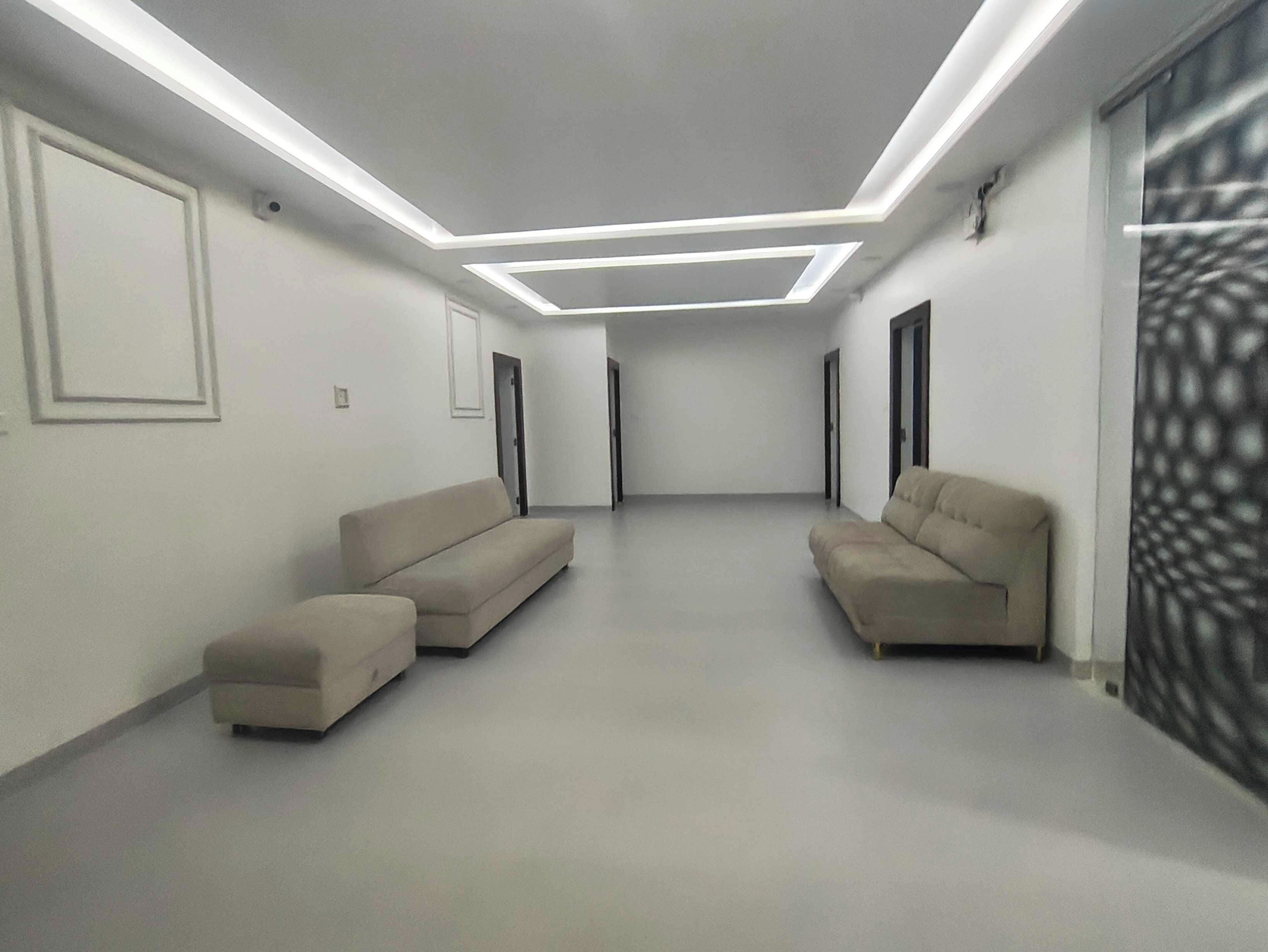 Quarto moderno e minimalista com dois sofás e um pequeno banquinho, parede estampada e iluminação embutida no teto.