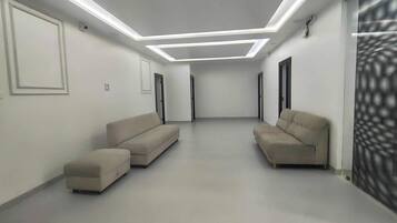 Quarto moderno e minimalista com dois sofás e um pequeno banquinho, parede estampada e iluminação embutida no teto.