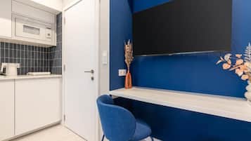 Cozinha moderna com bancada branca, uma cadeira azul e uma TV de tela plana presa em parede azul.
