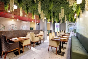 Interior de restaurante com várias mesas e cadeiras, um banco acolchoado verde e uma parede com textura.