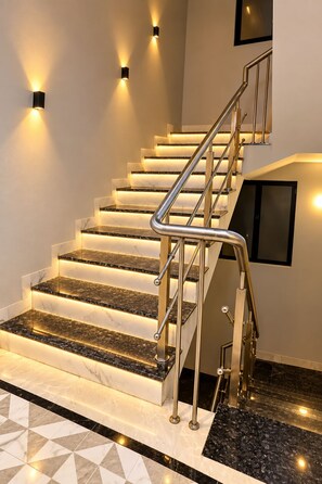 Escadaria com corrimão de metal, degraus de mármore e iluminação embutida na parede.